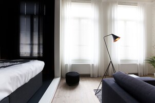 Um quarto moderno com uma cama, um abajur de chão e um pequeno banquinho.