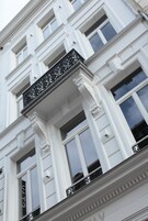 Um edifício com fachada branca, grandes janelas e grades de ferro decorativas.