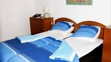 Quarto com duas camas, um tapete vermelho, um quadro na parede e uma mesinha de cabeceira com abajur e telefone.