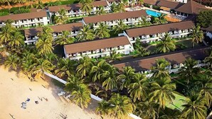Resort com várias construções tipo bangalô, praia e palmeiras.