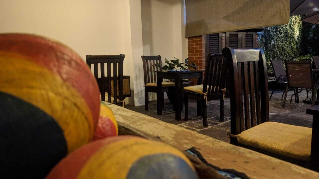 Uma área de refeições com cadeiras e mesas de madeira, um banco e um vaso de planta.