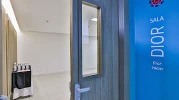 Entrada de um quarto de hotel com parede azul, porta com espelho e mesa com água engarrafada.
