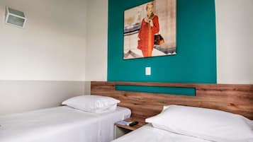 Quarto de hotel com duas camas de solteiro, uma cabeceira de madeira, uma parede de destaque azul-turquesa e um quadro com a imagem de uma pessoa num casaco vermelho.