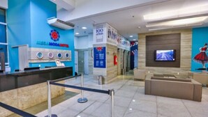 Um hall de hotel moderno com uma mesa de recepção, um ecrã digital e uma parede azul com um logótipo.