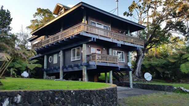 Uma casa de madeira de vários andares com uma varanda, cercada por vegetação.