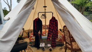 Tenda com cama, cadeira, mesa e um varal com roupas.