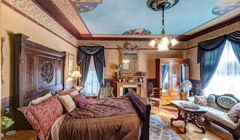 Quarto com uma cama grande, área de estar com sofá e uma mesa, e lareira.