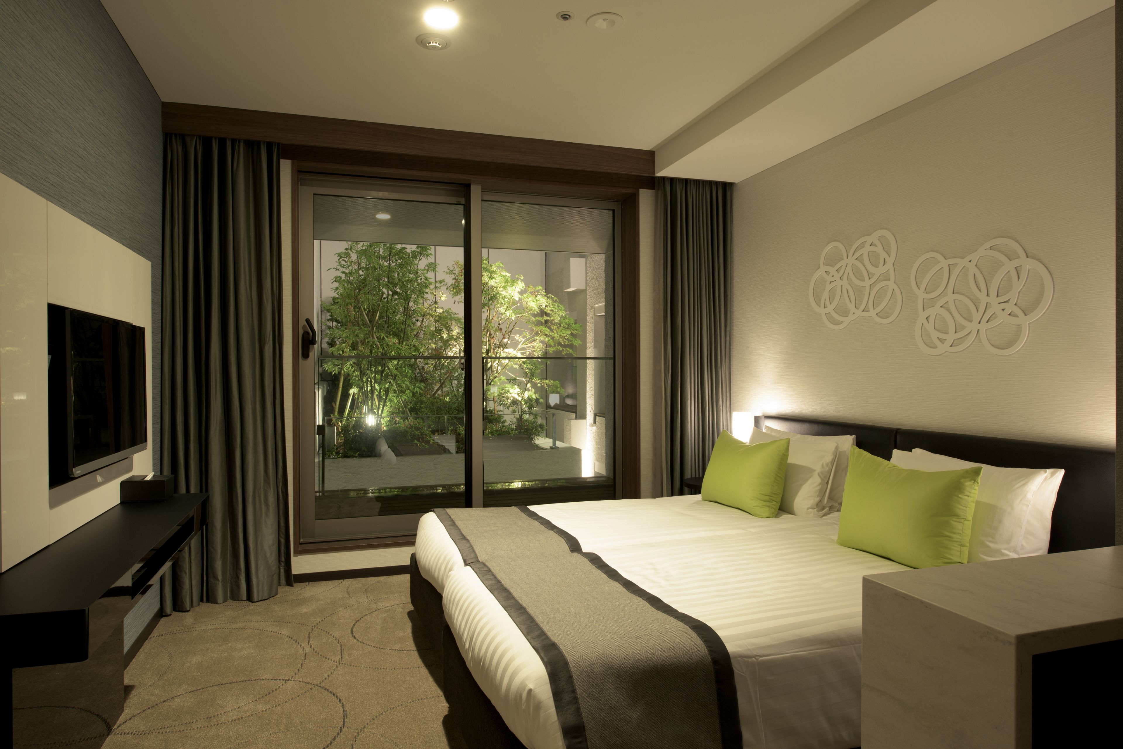 Quarto de hotel moderno com uma cama grande, televisão de tela plana e porta de vidro deslizante para uma varanda.