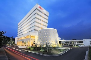 Um hotel moderno com um letreiro chamativo 'prima hotel', um edifício circular com janelas uniformemente espaçadas e uma área ajardinada bem cuidada com árvores.