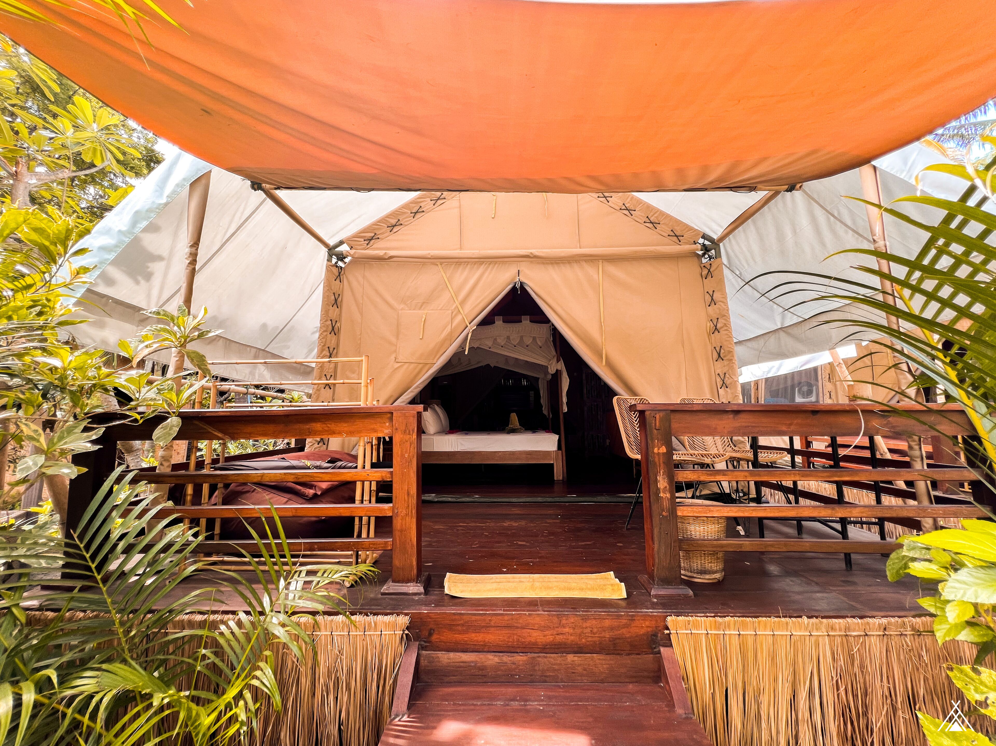 Alojamento em tenda com um alpendre de madeira, uma cama e vista para o verde ao redor.