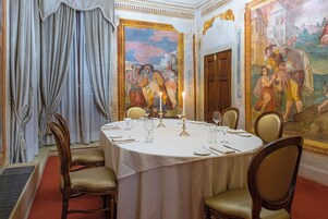 Uma sala de jantar com uma mesa redonda posta para seis pessoas, rodeada por cadeiras de madeira com assentos acolchoados.