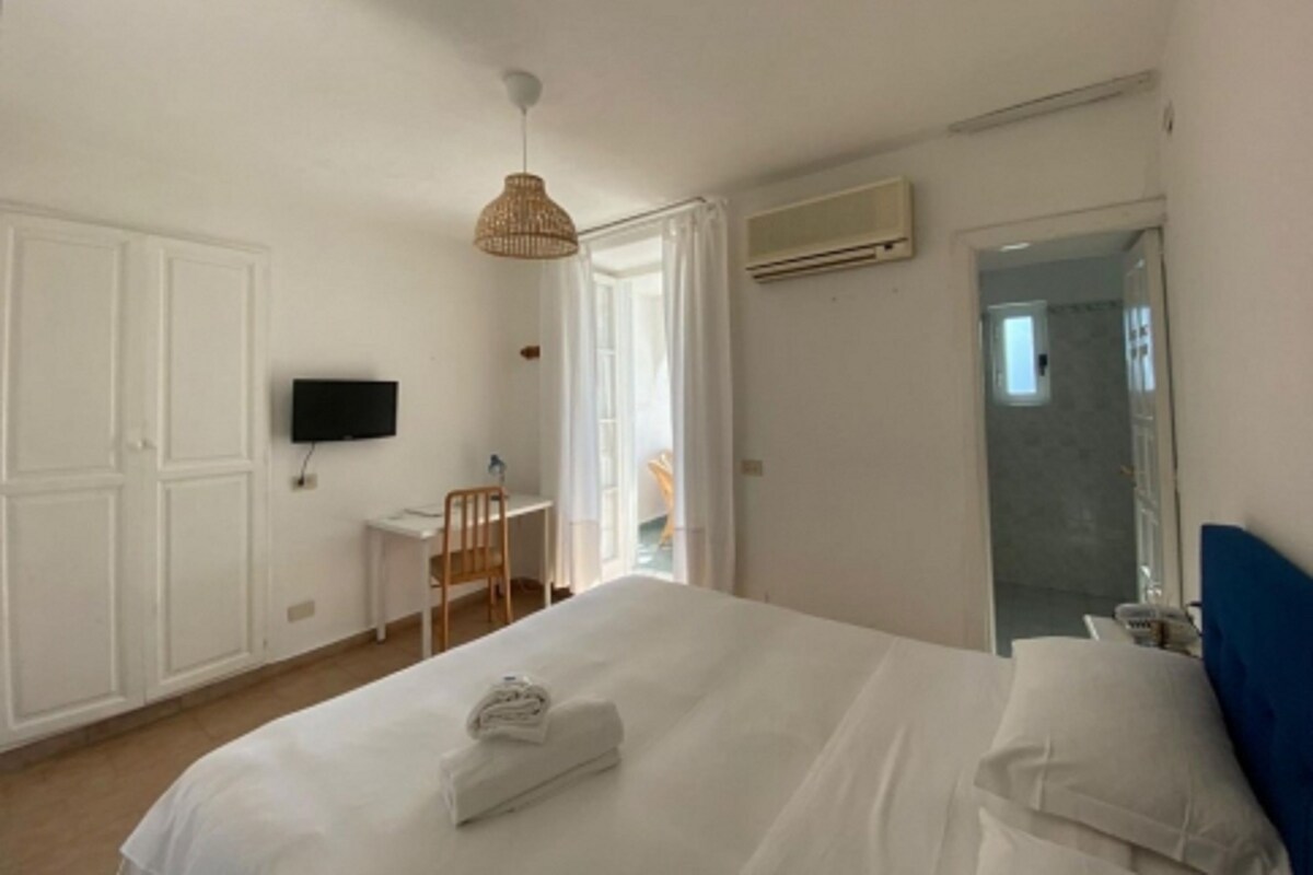Quarto de hotel com cama, escrivaninha, cadeira, televisão e ar condicionado.