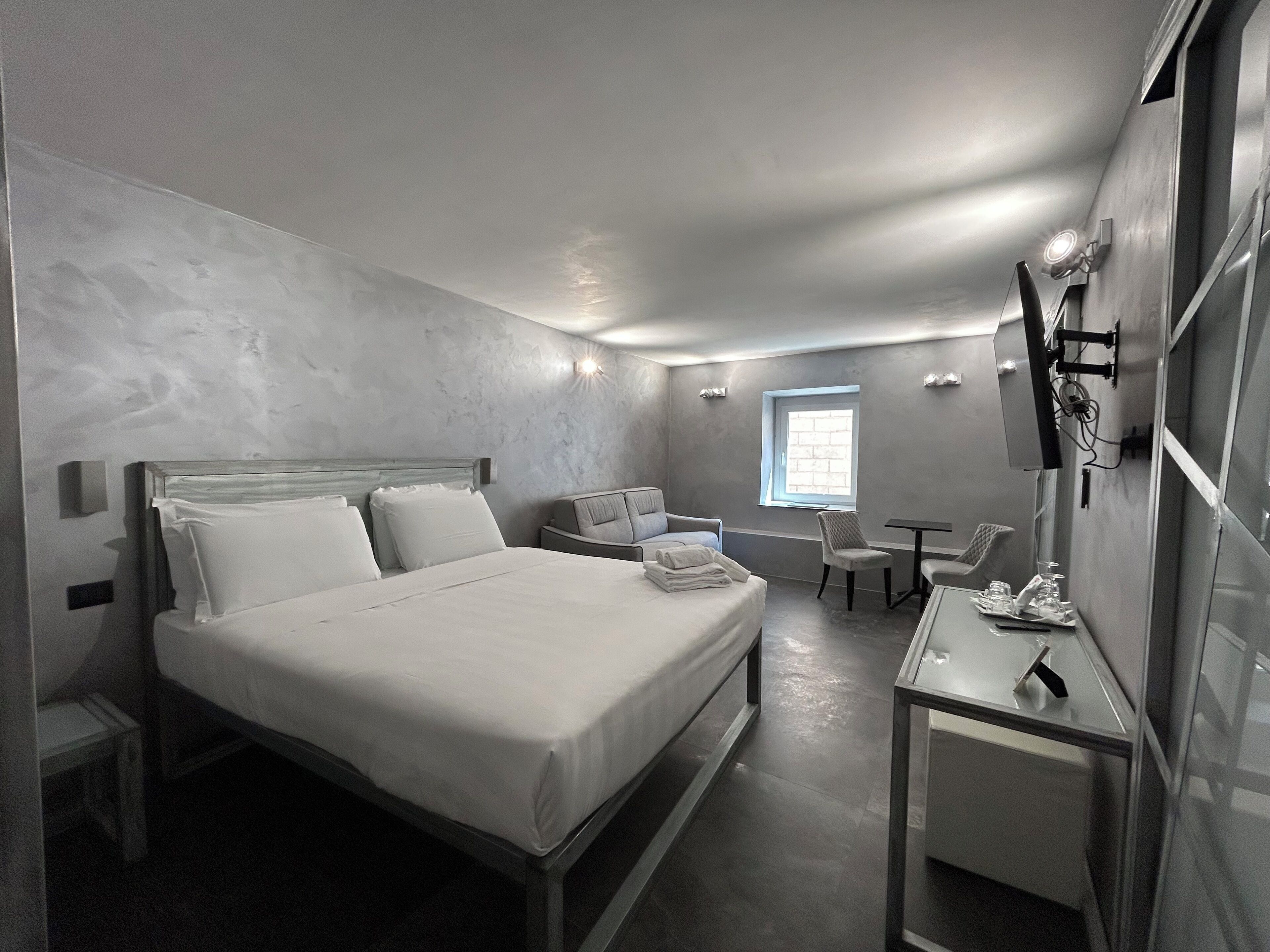 Quarto de hotel moderno com uma cama grande, uma escrivaninha, uma cadeira e uma mesinha.