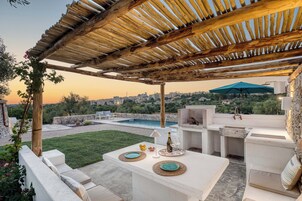 Um pátio externo com pérgola, piscina e área de refeições com mesa e cadeiras.