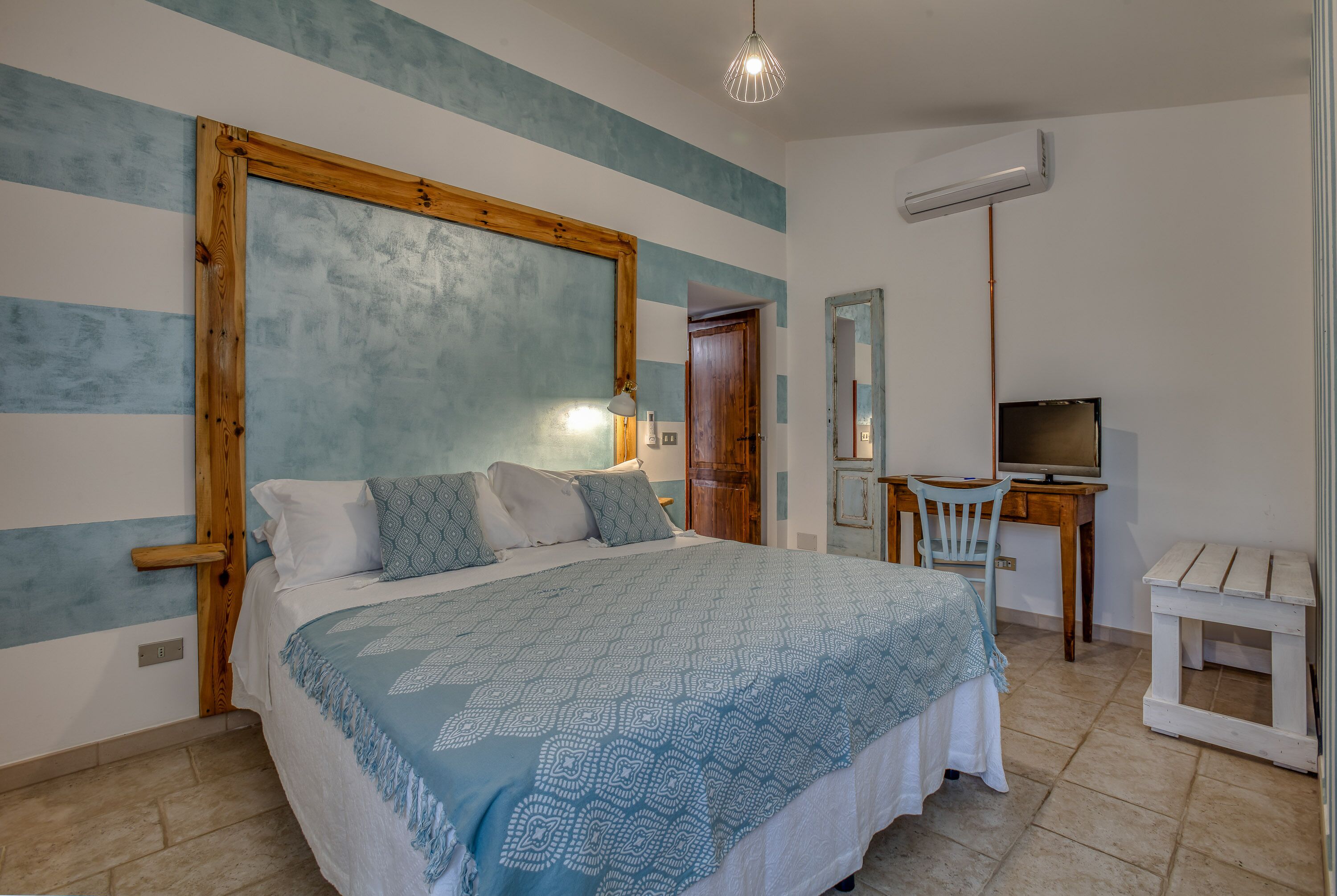 Quarto com cama, escrivaninha, cadeira e televisão.