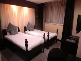 Quarto de hotel com duas camas de solteiro, uma escrivaninha com cadeira, televisão e janela com cortinas.