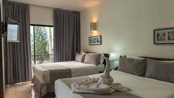 Quarto de hotel com duas camas, varanda com cortinas, luminária na parede e quadros emoldurados.