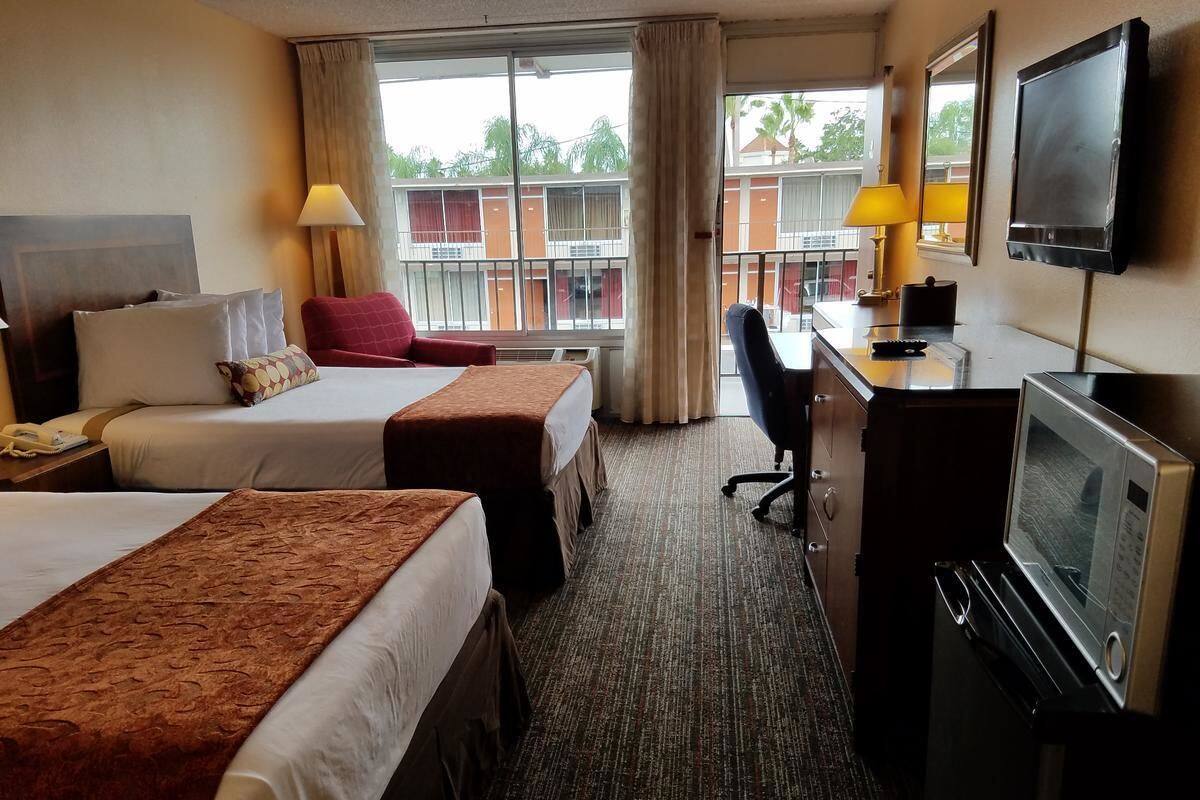 Quarto de hotel com duas camas, uma mesa de trabalho com uma televisão, micro-ondas e uma cadeira.