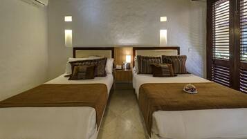 Quarto de hotel com duas camas de solteiro, cabeceira de madeira, mesa de cabeceira com abajur e janela com persianas.