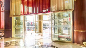 Um saguão de hotel com entrada de vidro, balcão de recepção e vista para a rua.