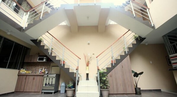 Interior espaçoso com uma escadaria central, área de cozinha com eletrodomésticos e plantas em vasos.