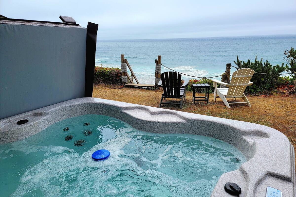 Uma banheira de hidromassagem com vista para o oceano, cercada por cadeiras e uma mesa.