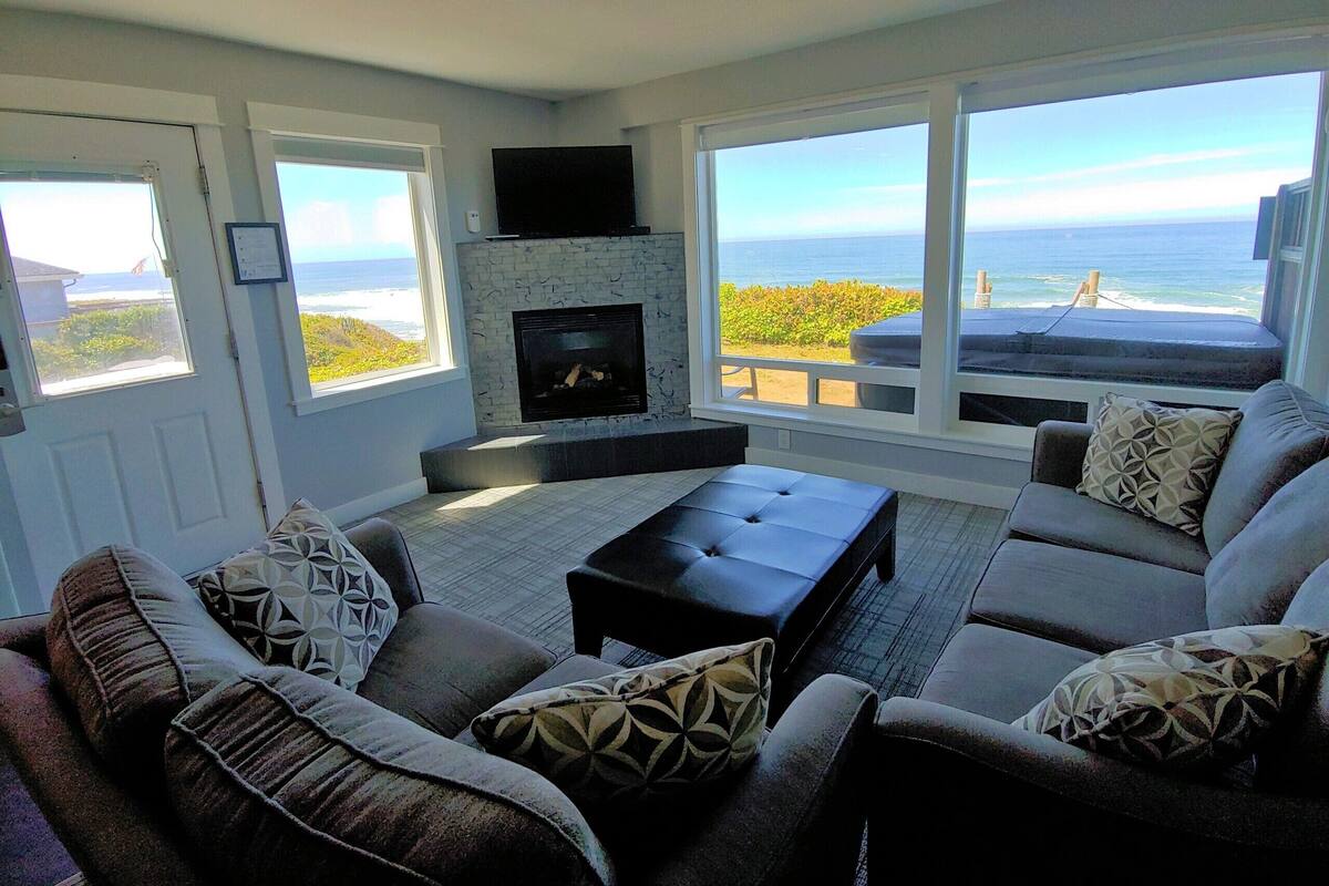 Uma sala de estar com lareira, grandes janelas com vista para o mar e um espaço de estar aconchegante.