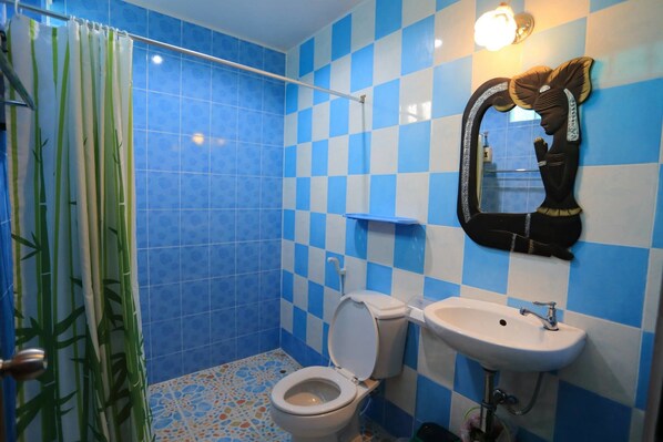 Casa de banho com parede revestida em azulejos azuis e brancos formando padrão xadrez, sanita branca, lavatório e cortina de chuveiro com motivos de bambu.