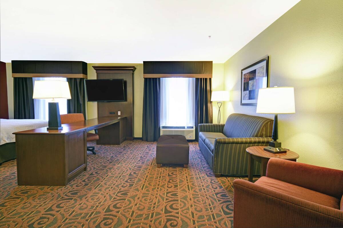 Quarto de hotel com cama, escrivaninha, cadeira, sofá e pequena mesa com abajur.
