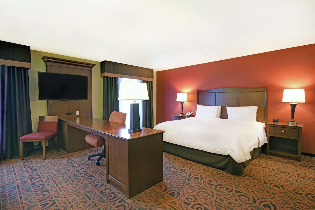 Quarto de hotel com cama, escrivaninha, cadeira e duas luminárias de cabeceira.