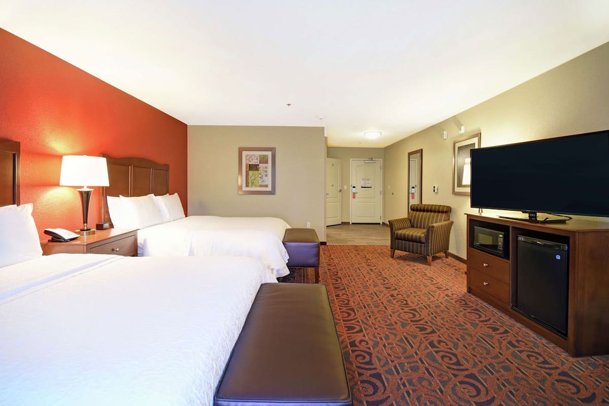Quarto de hotel com duas camas, uma escrivaninha, uma cadeira, uma televisão e um micro-ondas.