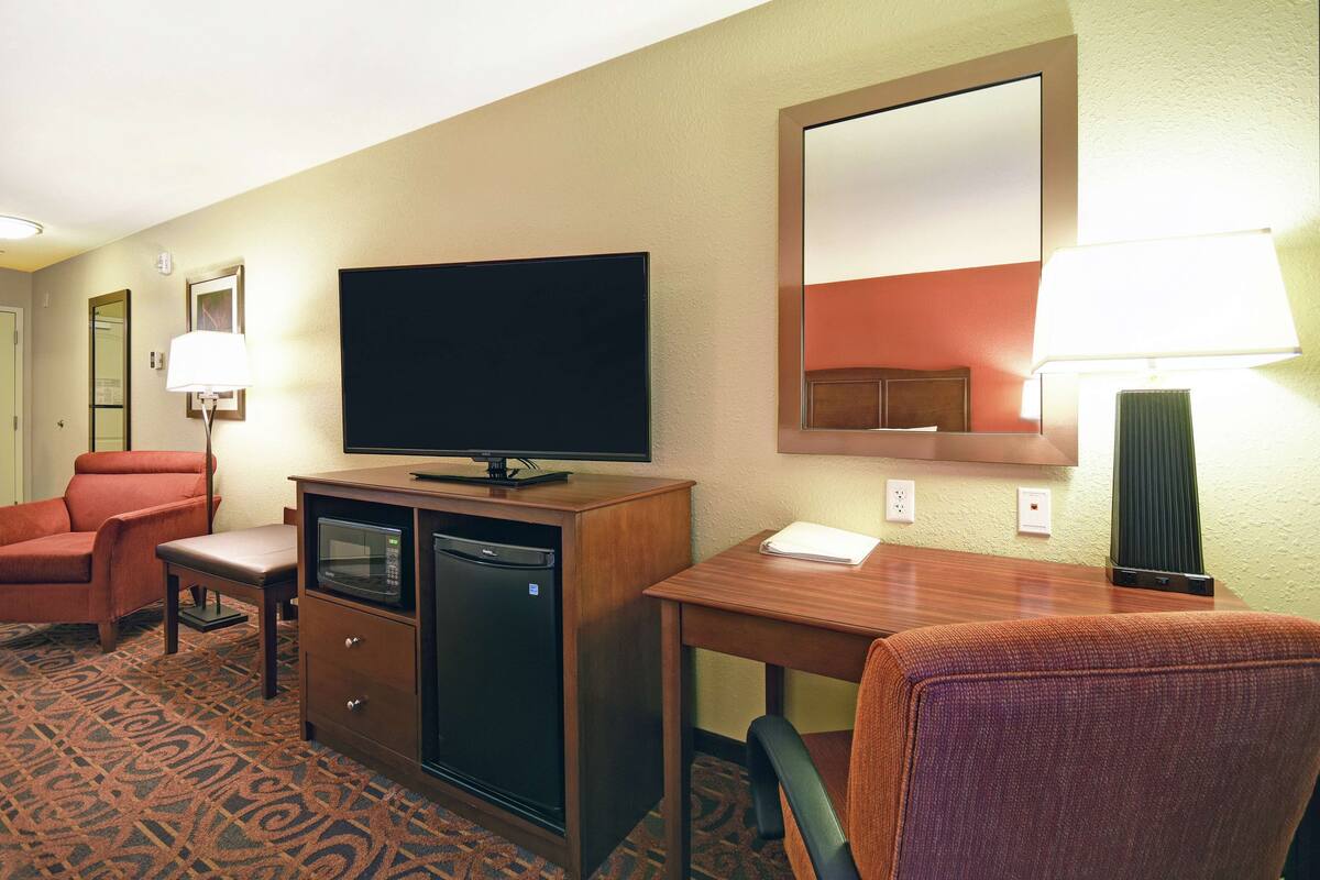 Quarto de hotel com televisão, escrivaninha, cadeira, micro-ondas e um pequeno frigorífico.