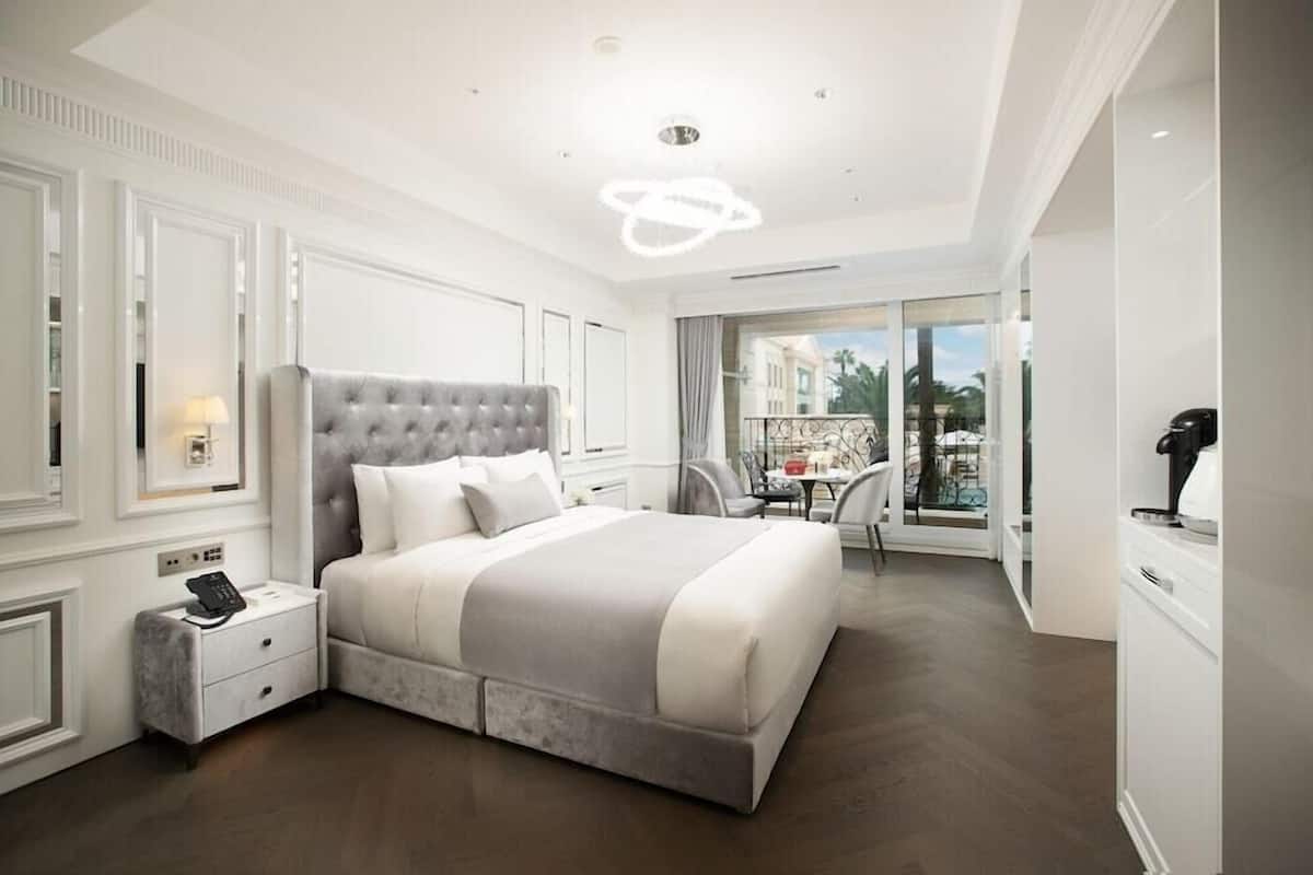 Quarto de hotel moderno com uma cama grande, uma mesinha de cabeceira, uma cadeira e uma varanda com vista.