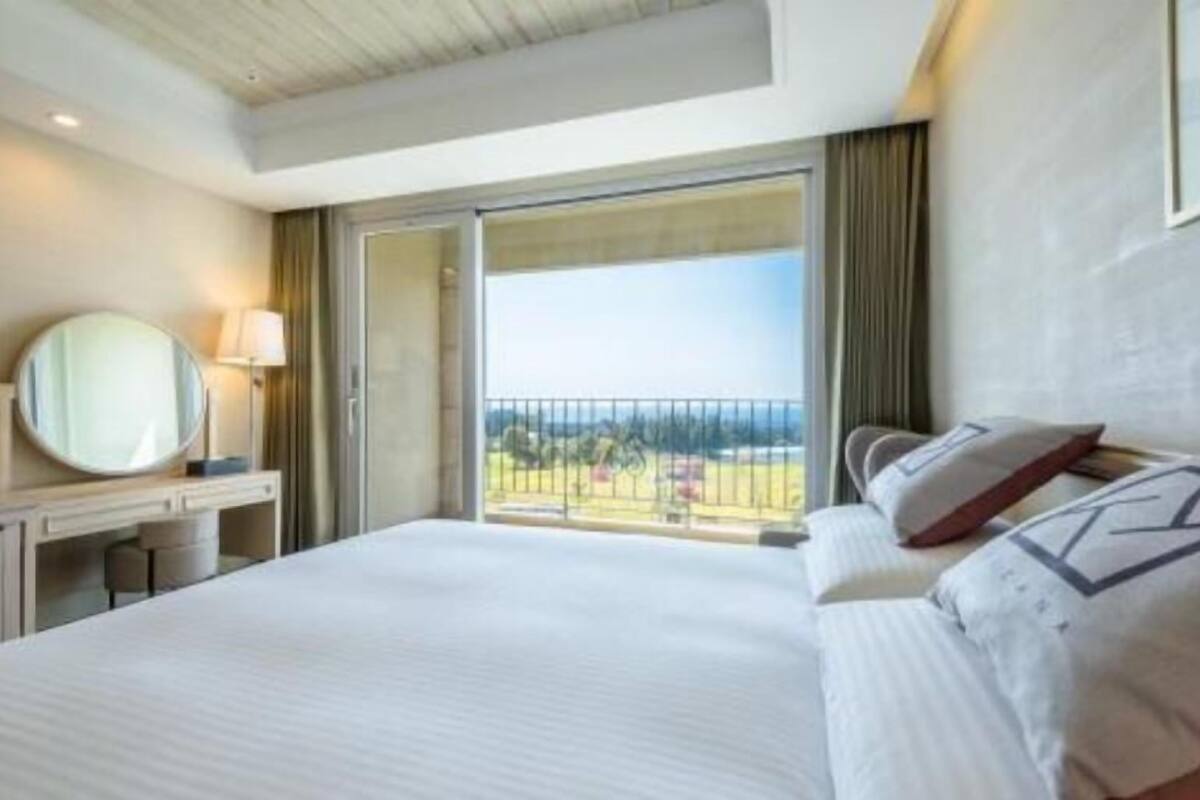 Quarto de hotel com uma cama grande, uma mesa com abajur, um espelho redondo e uma varanda com vista.