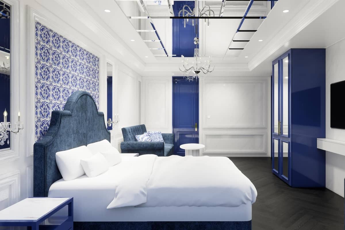 Quarto de hotel moderno com uma cama grande, área de estar, televisão e lustre.