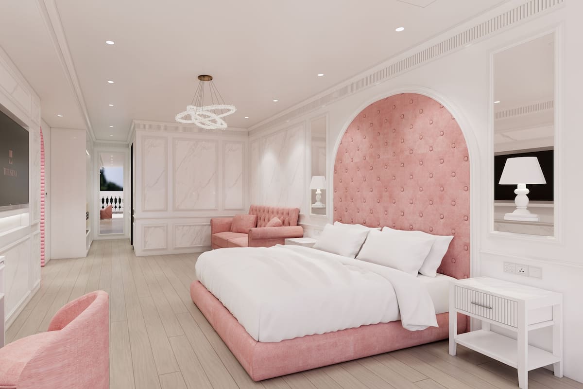 Quarto com cama grande, poltrona rosa estofada, penteadeira com espelho e televisão.
