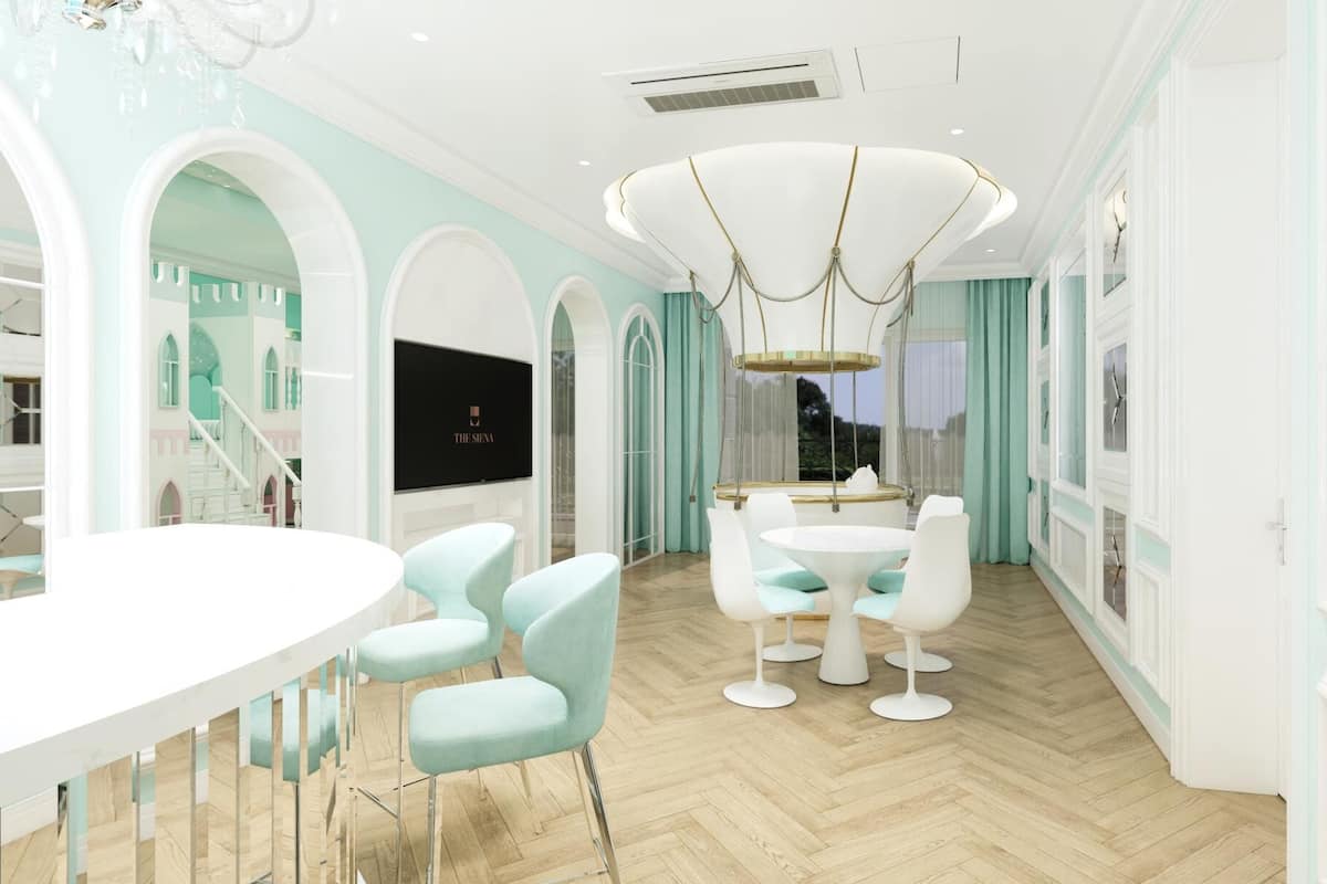 Um interior moderno com uma mesa redonda central e cadeiras, uma televisão na parede e um candelabro.
