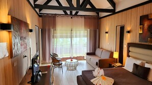 Quarto de hotel moderno com teto de madeira, sofá, cama, escrivaninha e cadeira.