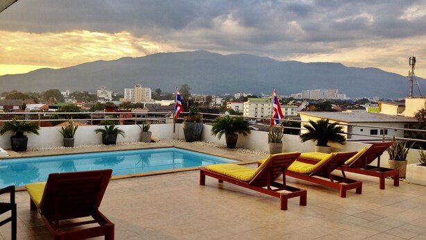 Área de piscina no terraço com espreguiçadeiras e plantas em vasos, com vista para a paisagem urbana e montanhas.