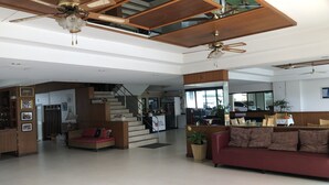 Uma sala de estar espaçosa com um sofá vermelho, uma mesa de centro de madeira e um ventilador de teto. Uma escada leva a um andar superior, e há vista para o exterior através de grandes janelas.