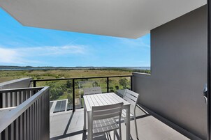 Uma varanda com mesa e cadeiras brancas, com vista para uma paisagem verde e colinas ao longe.