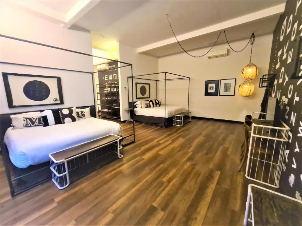 Quarto de hotel moderno com piso de madeira, uma cama grande com estrutura metálica, uma pequena mesa de cabeceira e um guarda-roupa com espelho.