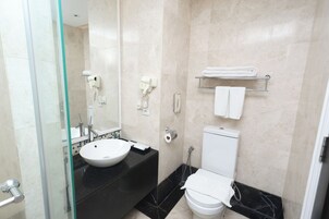 Casa de banho com cabine de duche em vidro, lavatório branco, bancada preta, sanita branca, porta-toalhas e espelho.