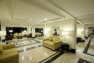 Um hall amplo com um sofá bege, poltronas e uma mesa de centro.