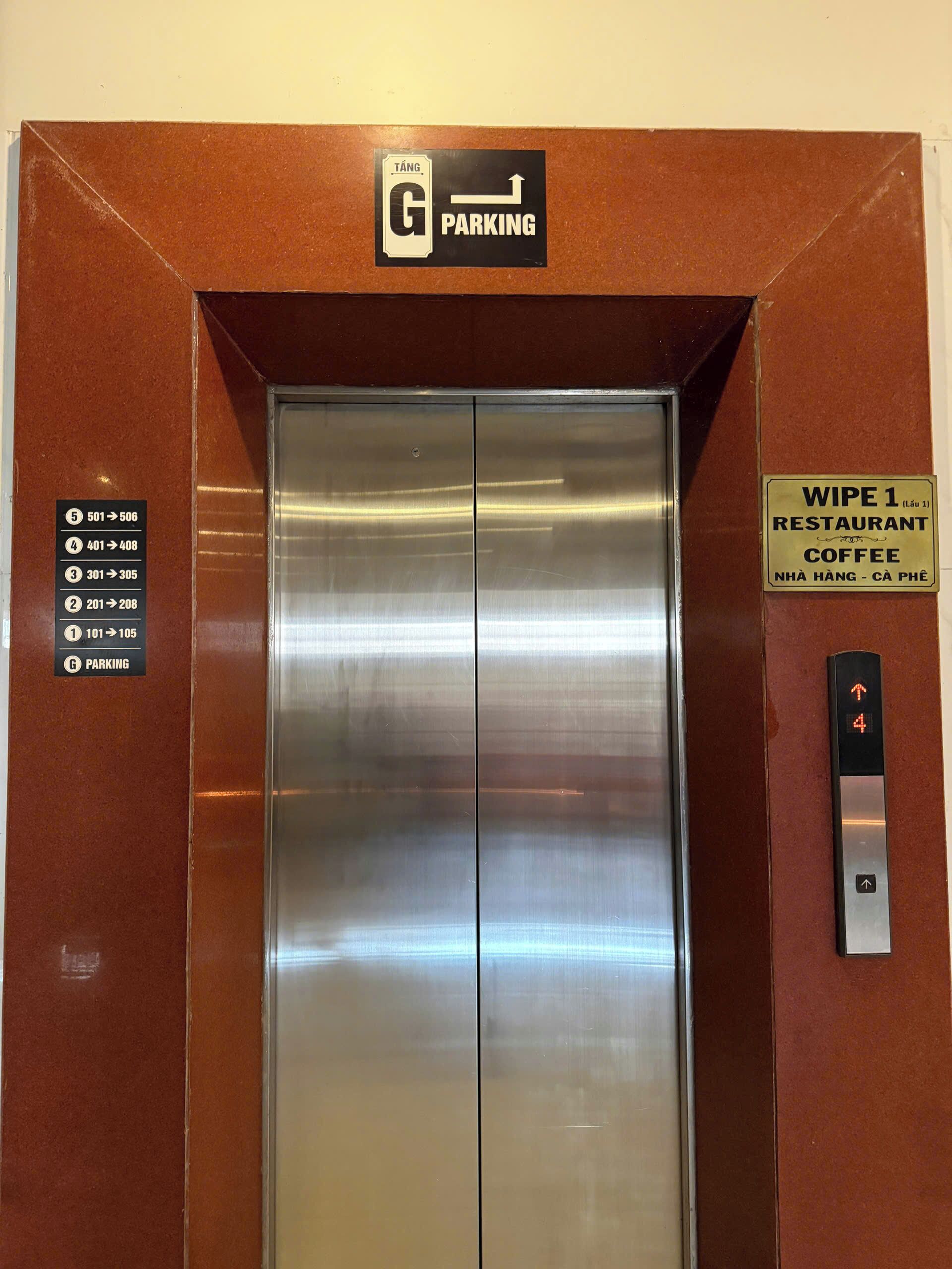 Um elevador com uma placa indicando os níveis de estacionamento 5 a 6, um restaurante chamado Wipe 1, e um visor digital mostrando o número do andar 4.