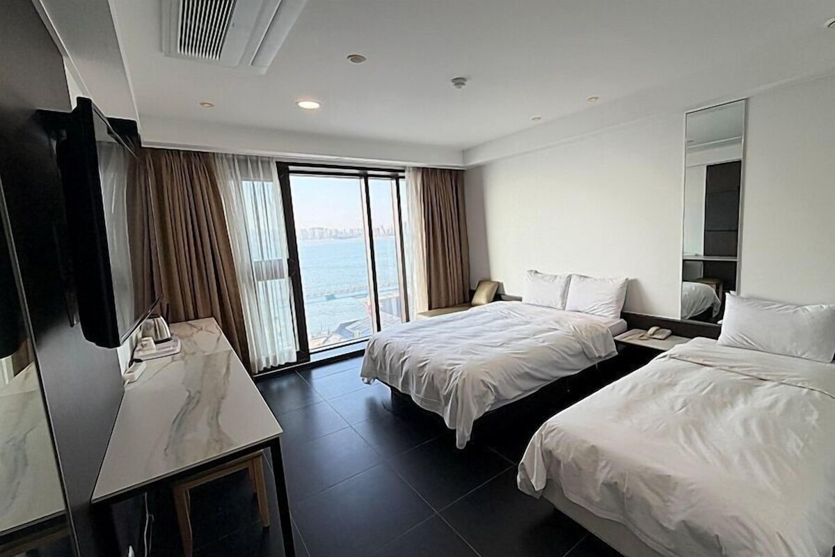 Quarto de hotel com duas camas, uma escrivaninha, um telefone e vista para a cidade.
