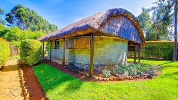 Uma cabana com telhado de palha e base de pedra, rodeada por um jardim bem cuidado e um caminho de pedra.