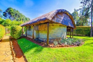 Uma cabana com telhado de palha e base de pedra, rodeada por um jardim bem cuidado e um caminho de pedra.