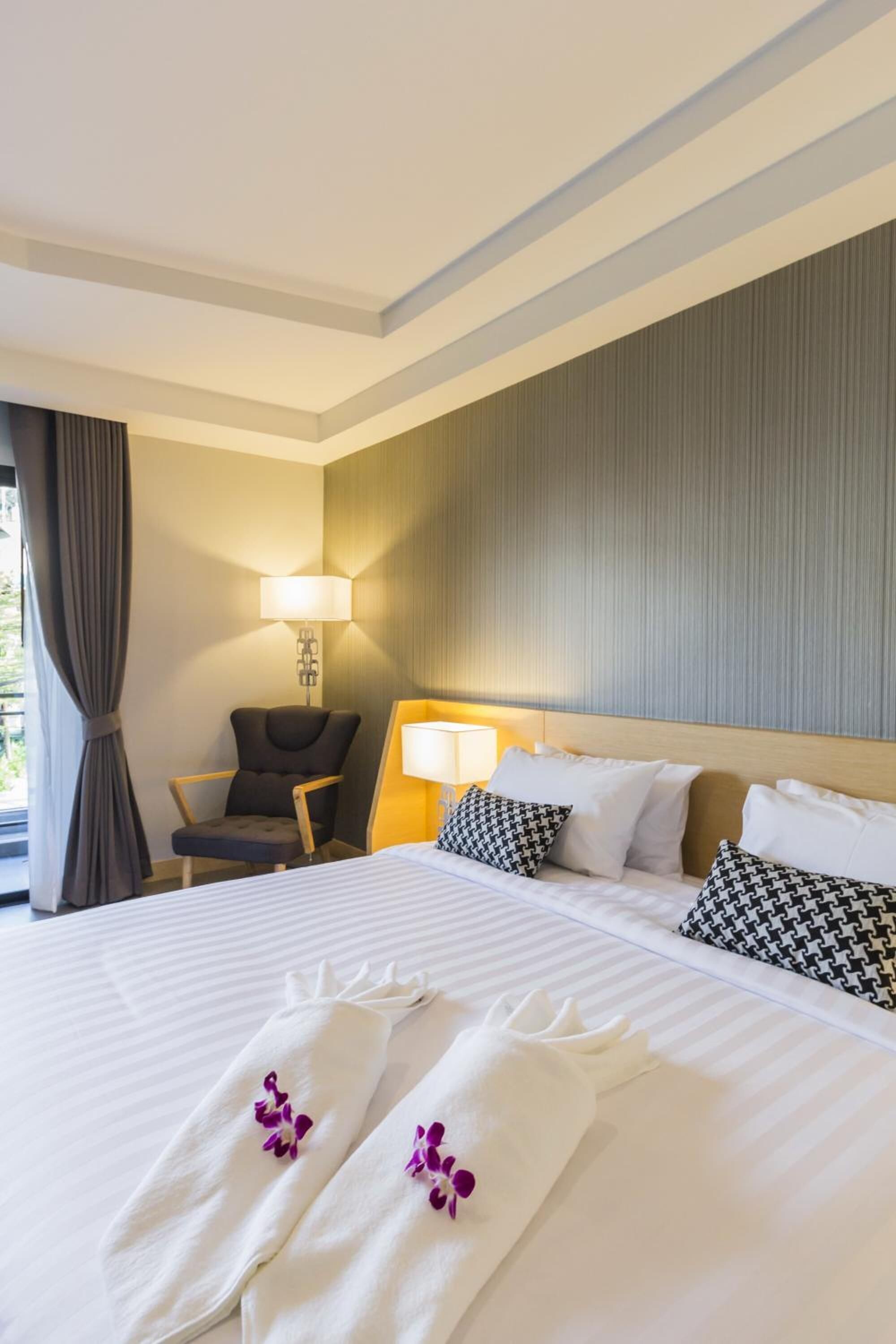 Quarto de hotel com uma cama grande, duas mesas de cabeceira, uma cadeira, um abajur e vista para o exterior.