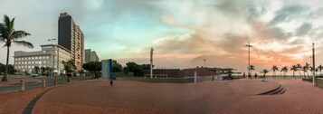 Uma passarela pavimentada com palmeiras, um edifício alto e um céu nublado.